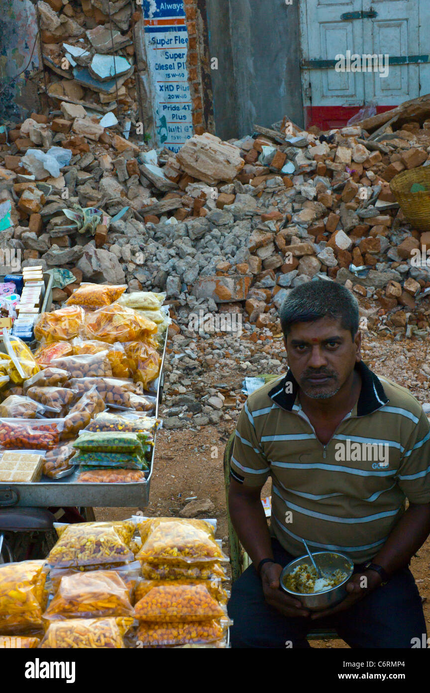 A man selling snacks in front of a house in shambles in Mysore ...