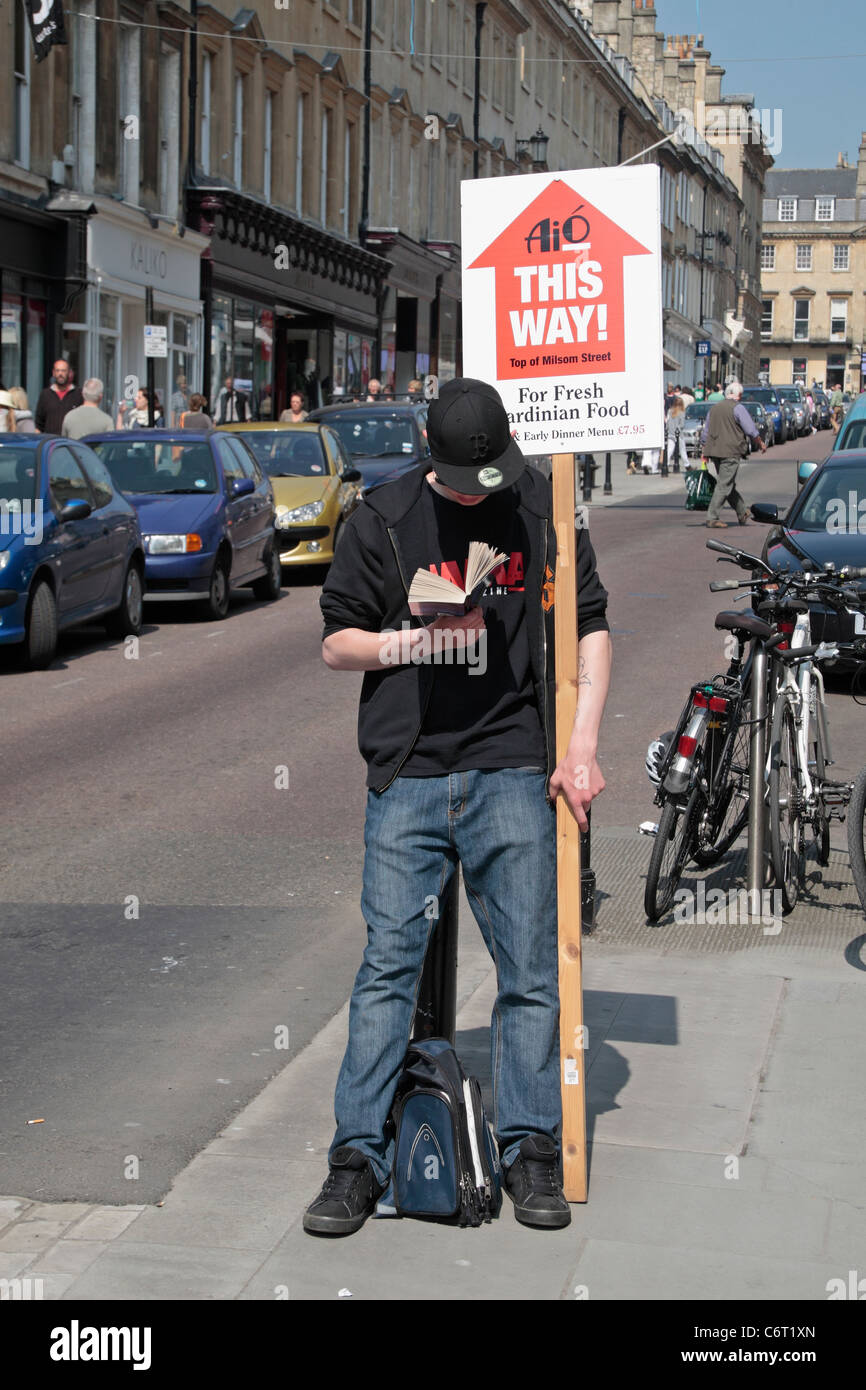 Man reading a book while holding a board advertising the Aio restaurant ...