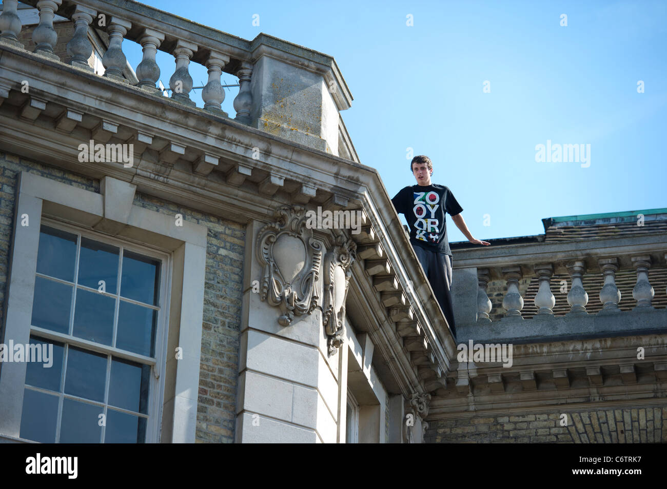 A young male, urban runner, walking along balustrade on roof of tall ...