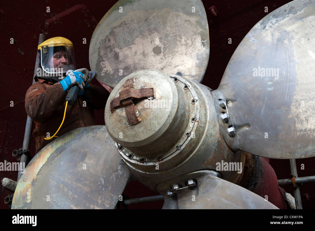 A shipyard worker wearing a safety visor on his face working on a ships ...