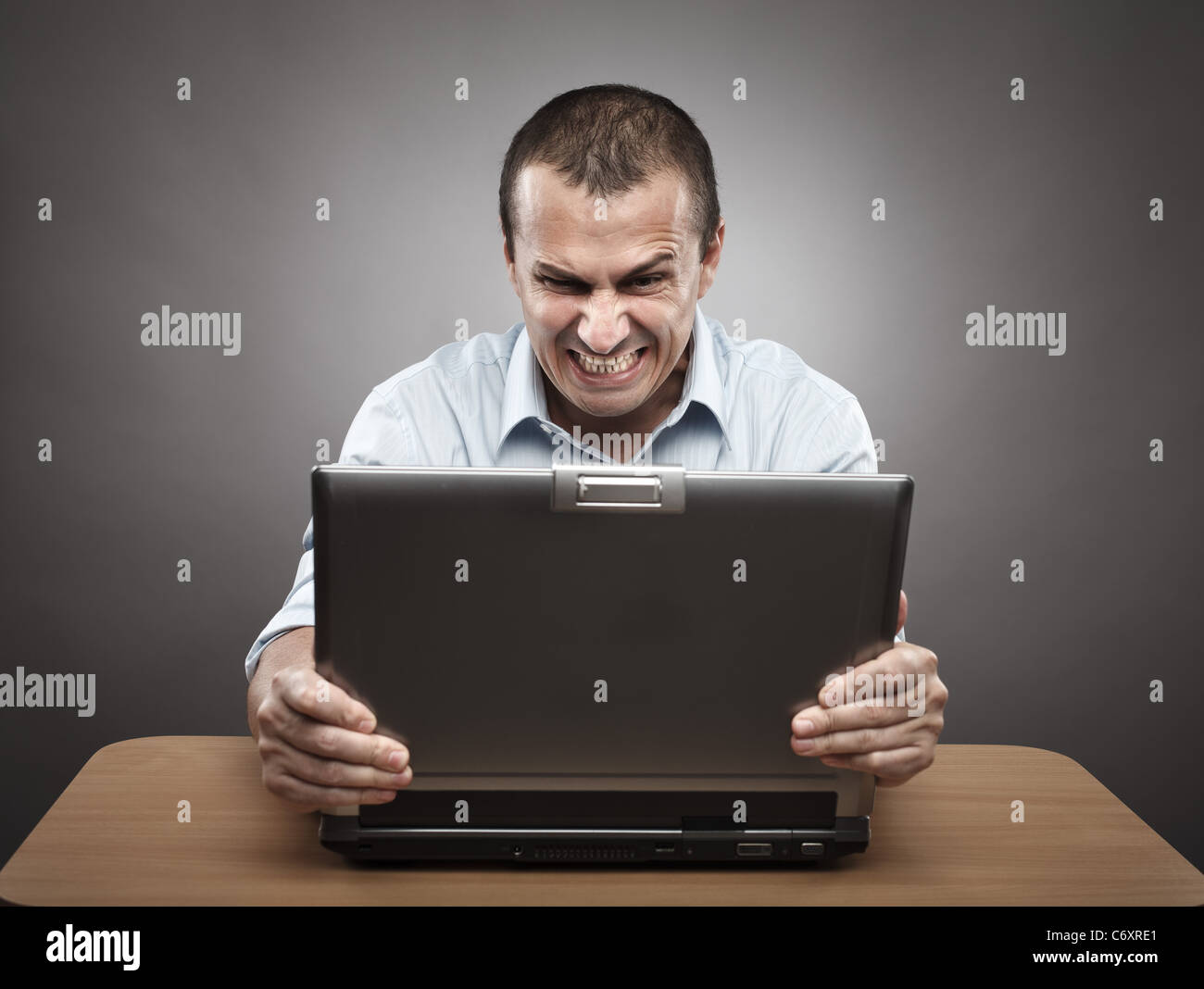 Portrait of an angry businessman at his laptop, on gray background ...