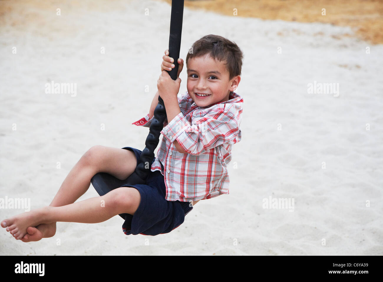 Boy playing on swing at playground Stock Photo - Alamy