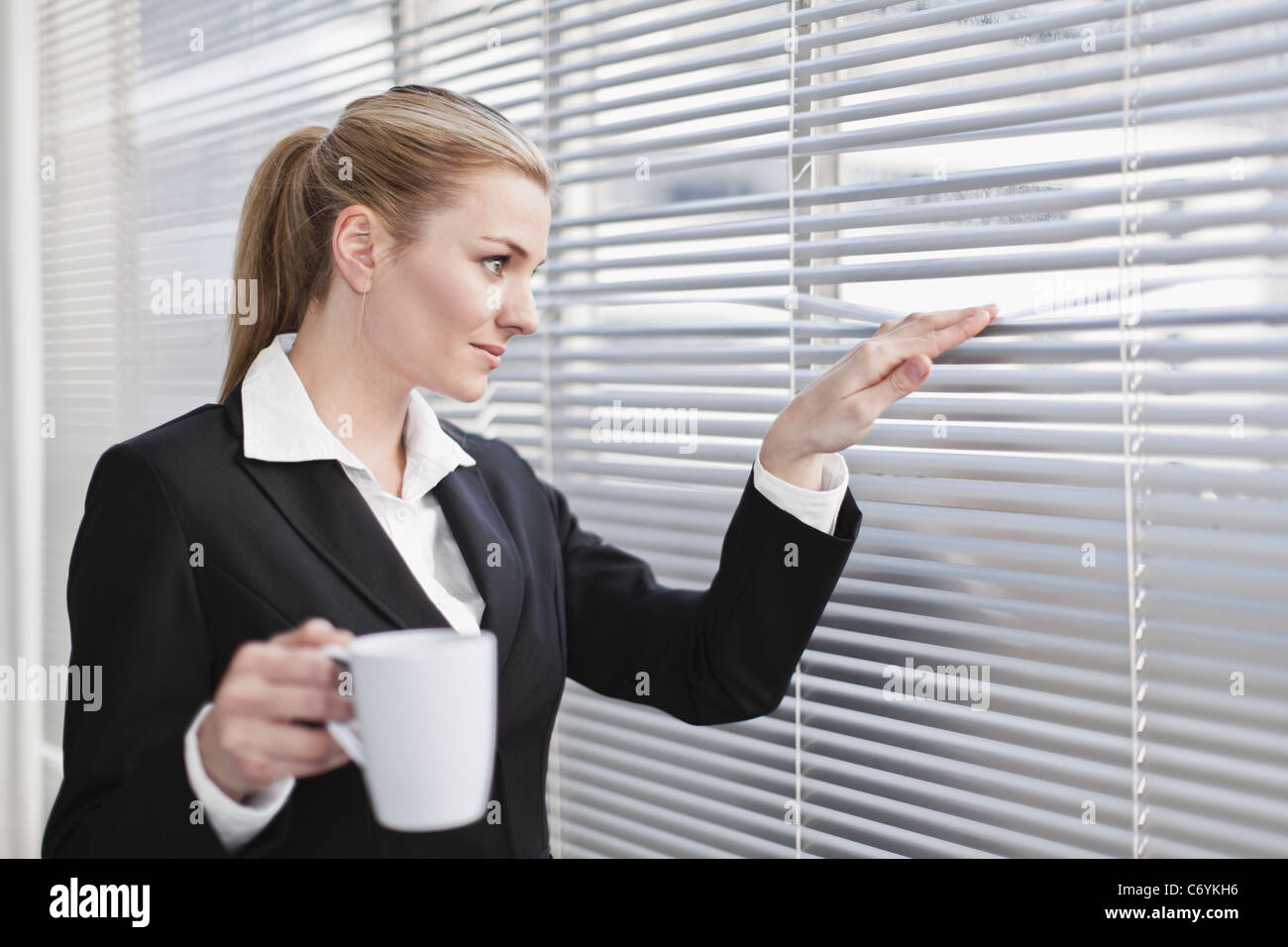 Businesswoman peering out of blinds Stock Photo - Alamy