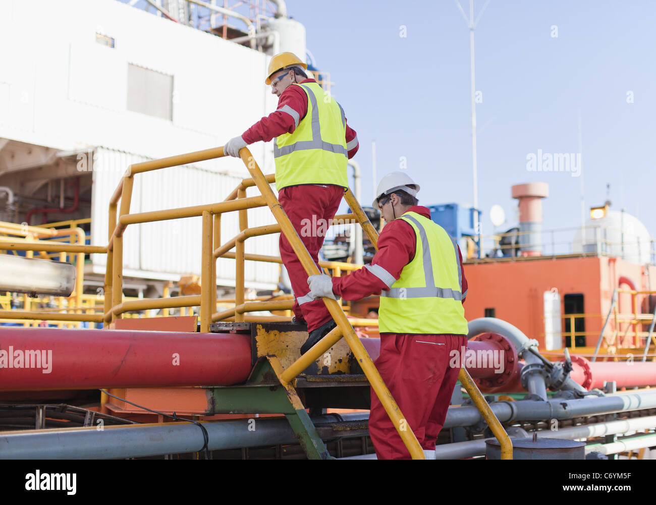 Workers climbing over pipes on oil rig Stock Photo - Alamy