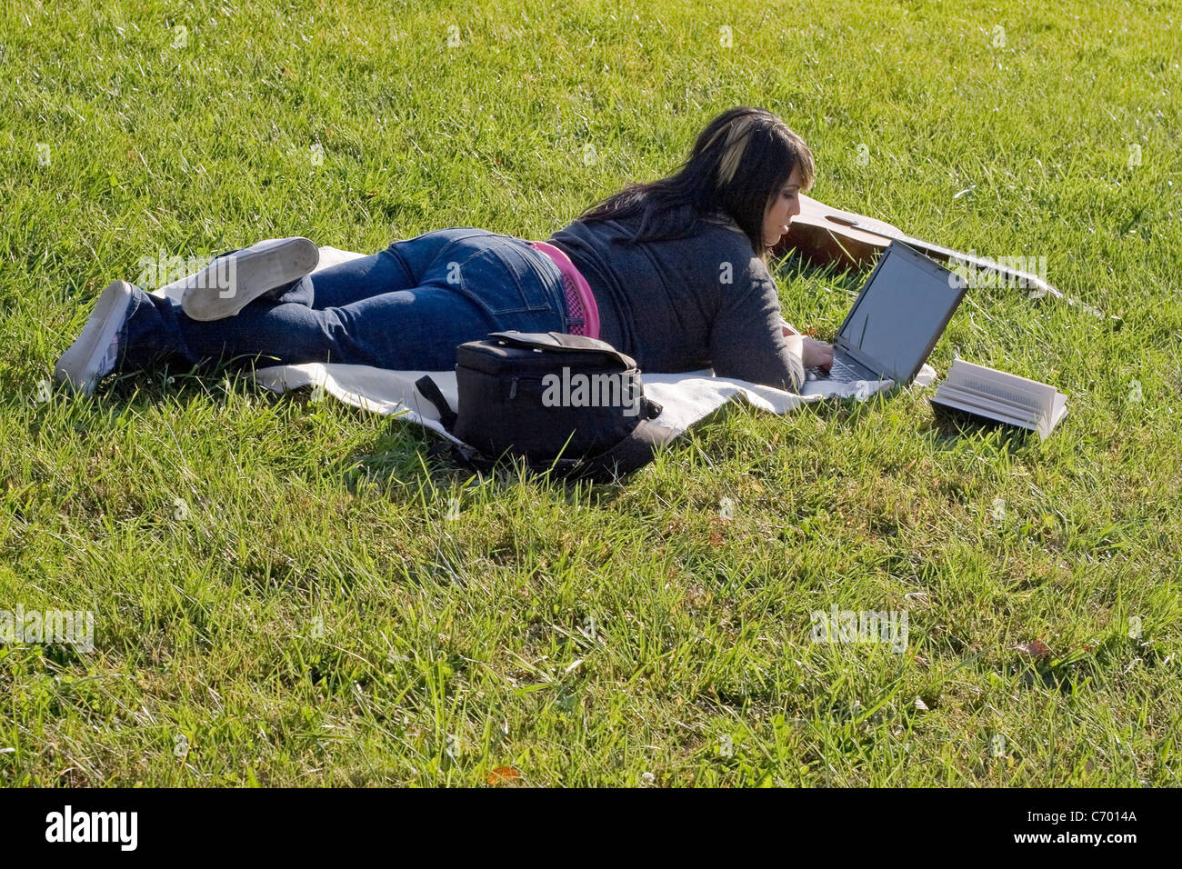 A young student using her laptop computer while laying in the grass on ...