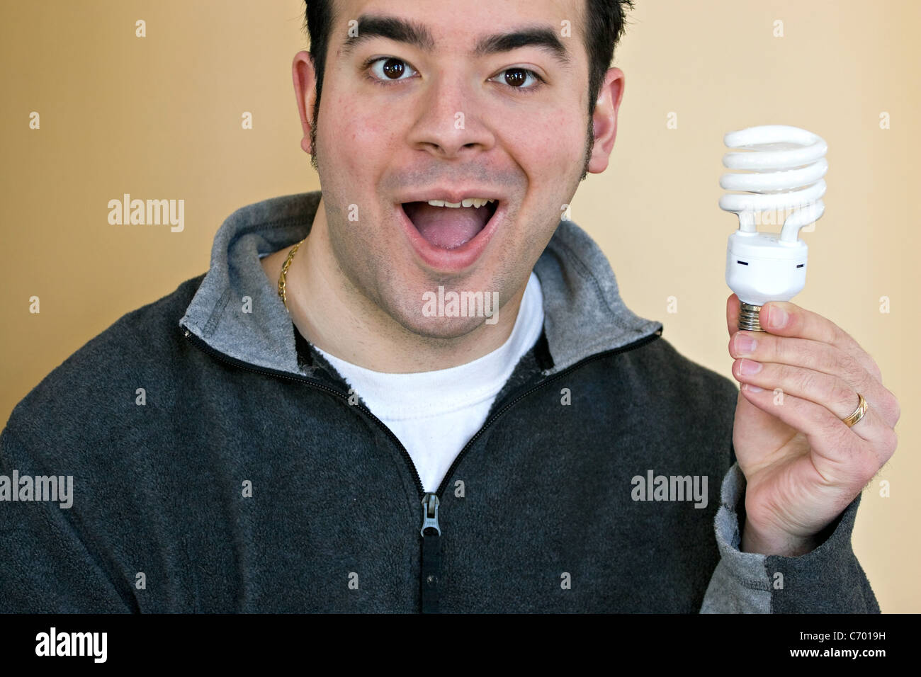 A young man holding an energy saving compact fluorescent light bulb ...