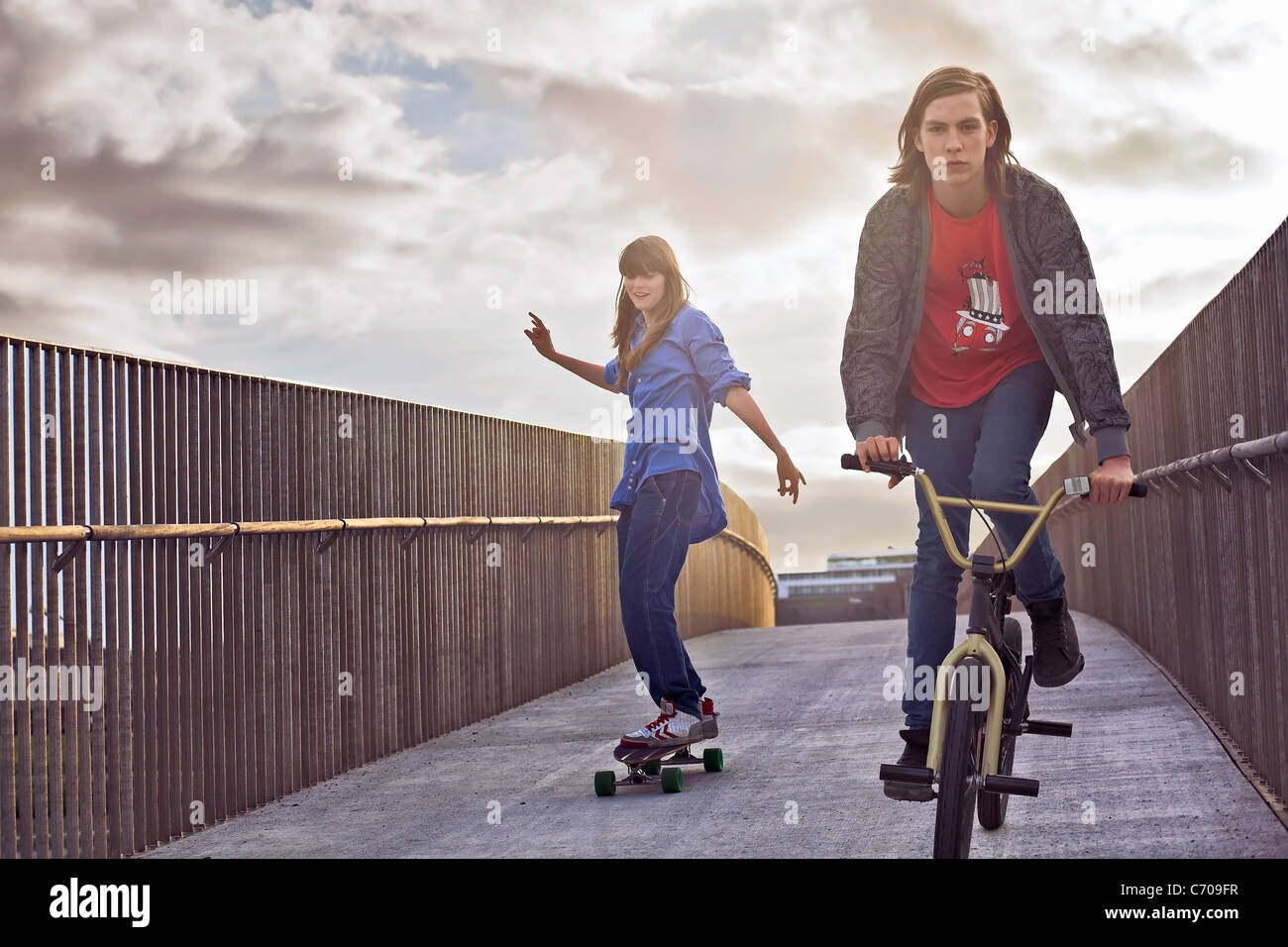 Teenagers riding bicycle and skateboard Stock Photo - Alamy