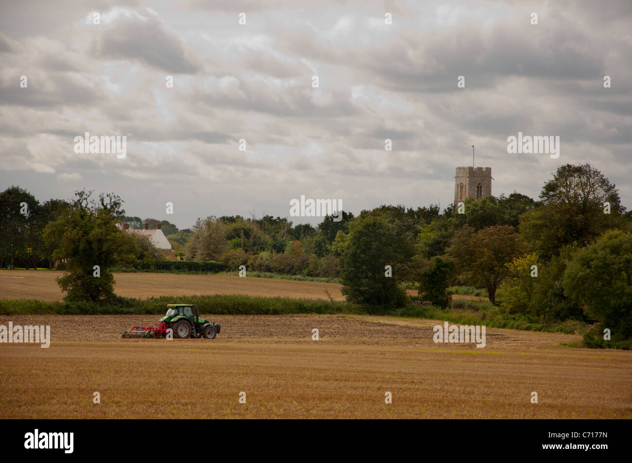 Tractor working in Norfolk Field with church Stock Photo - Alamy