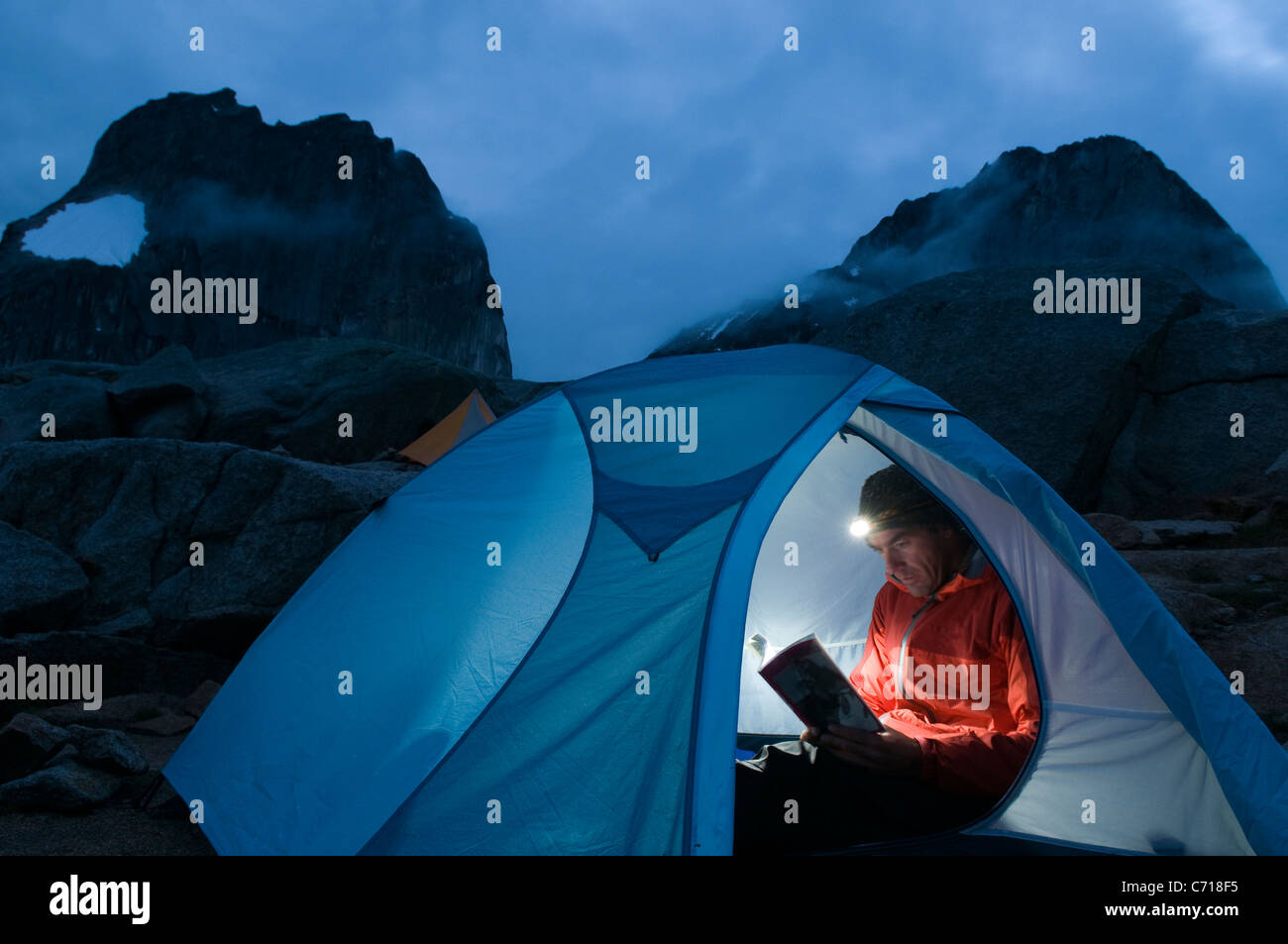 Man reading guidebook by headlamp in tent, Bugaboo Provincial Park ...