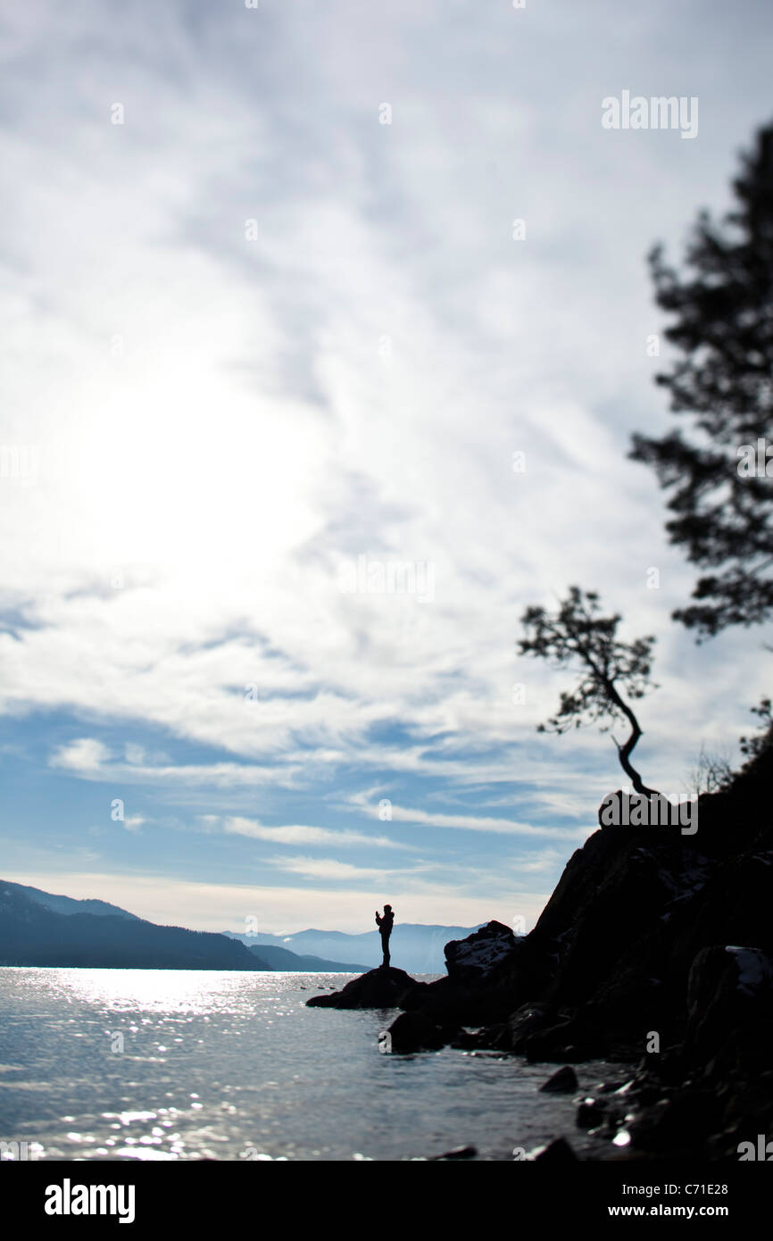 A male figure stands meditating on a rock with glimmering water in ...