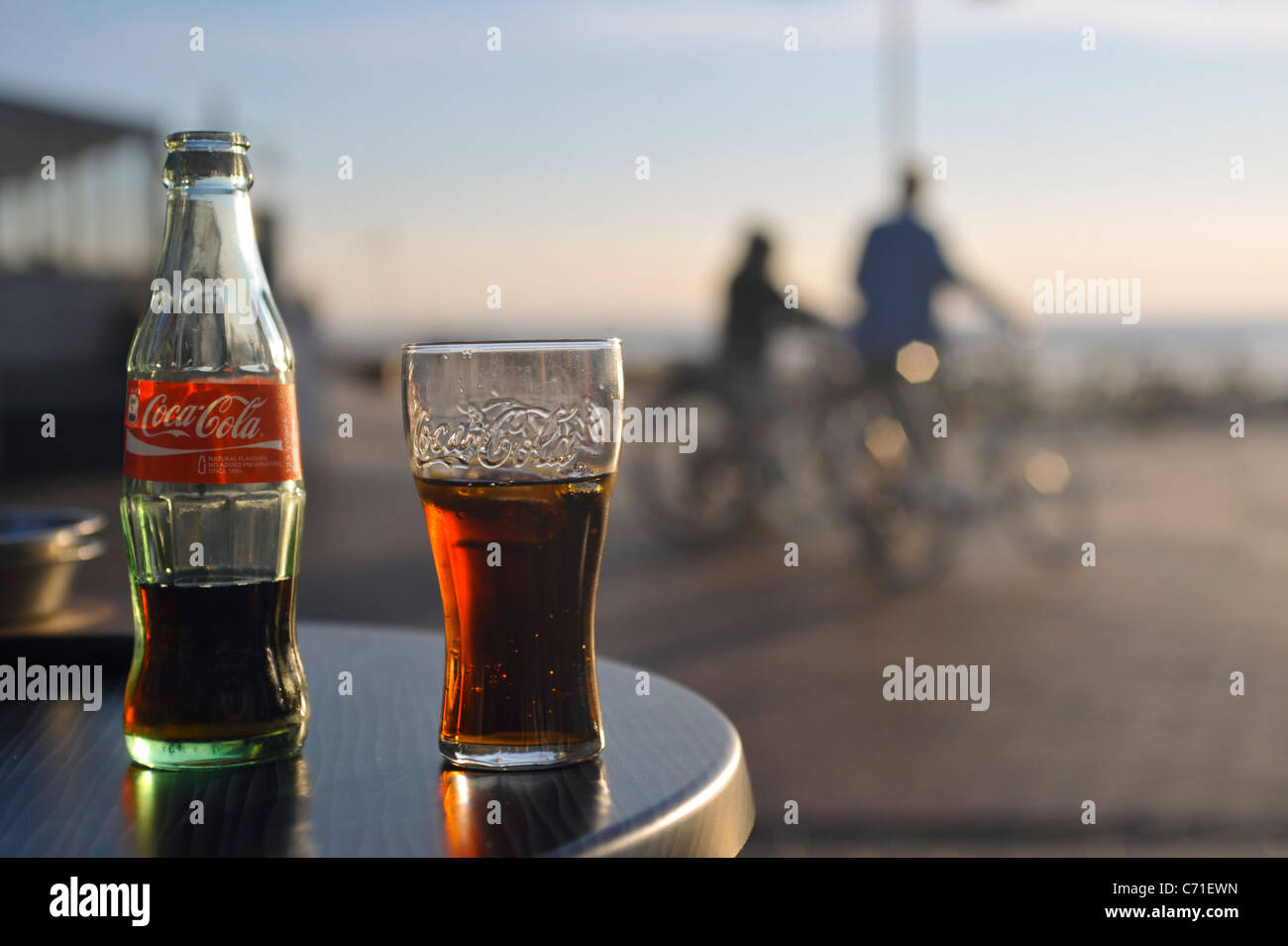 Glass of Coca Cola with bottle and couple with bikes in the background ...