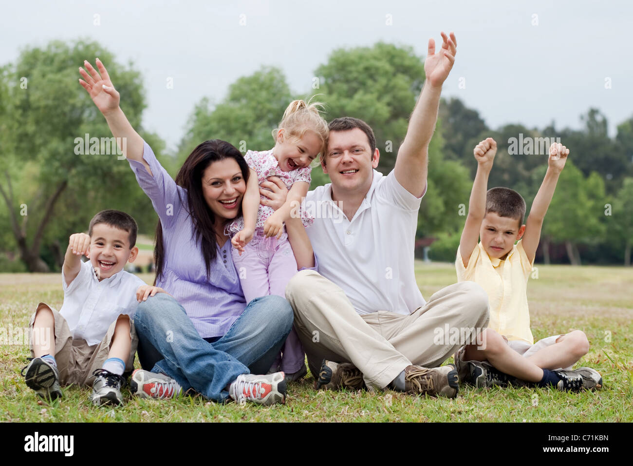 Happy family of five having fun by raising hands on the green land over ...