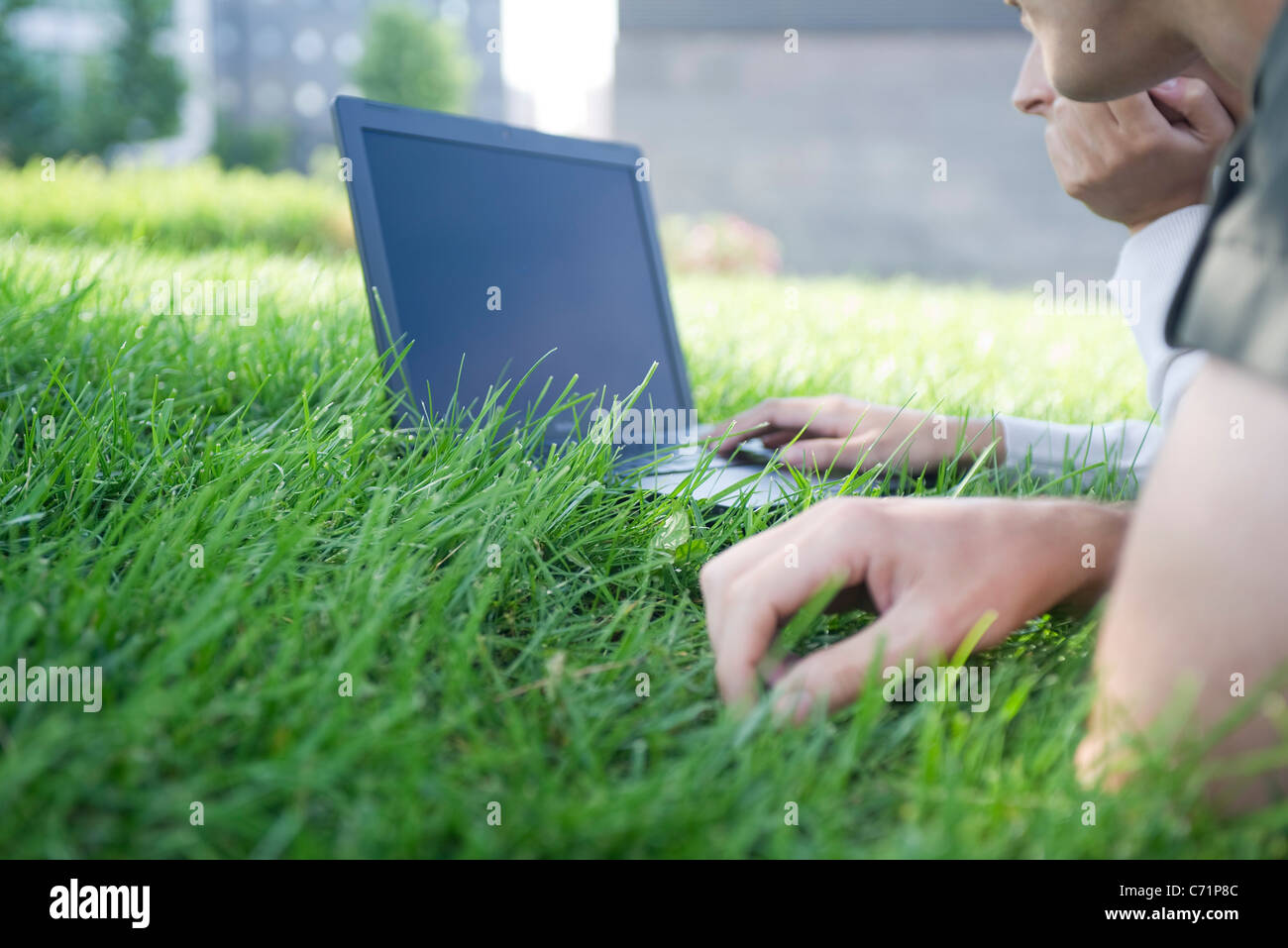 People using laptop computer while lying on grass, cropped Stock Photo ...