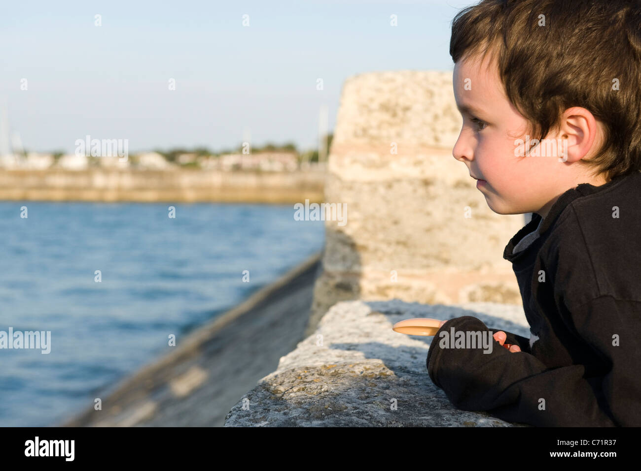 Little boy leaning against stone wall, looking at ocean view Stock ...