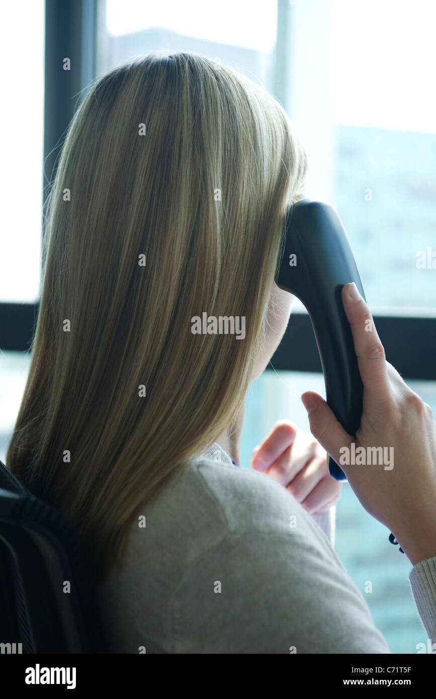 Woman looking out window while talking on landline phone, rear view ...