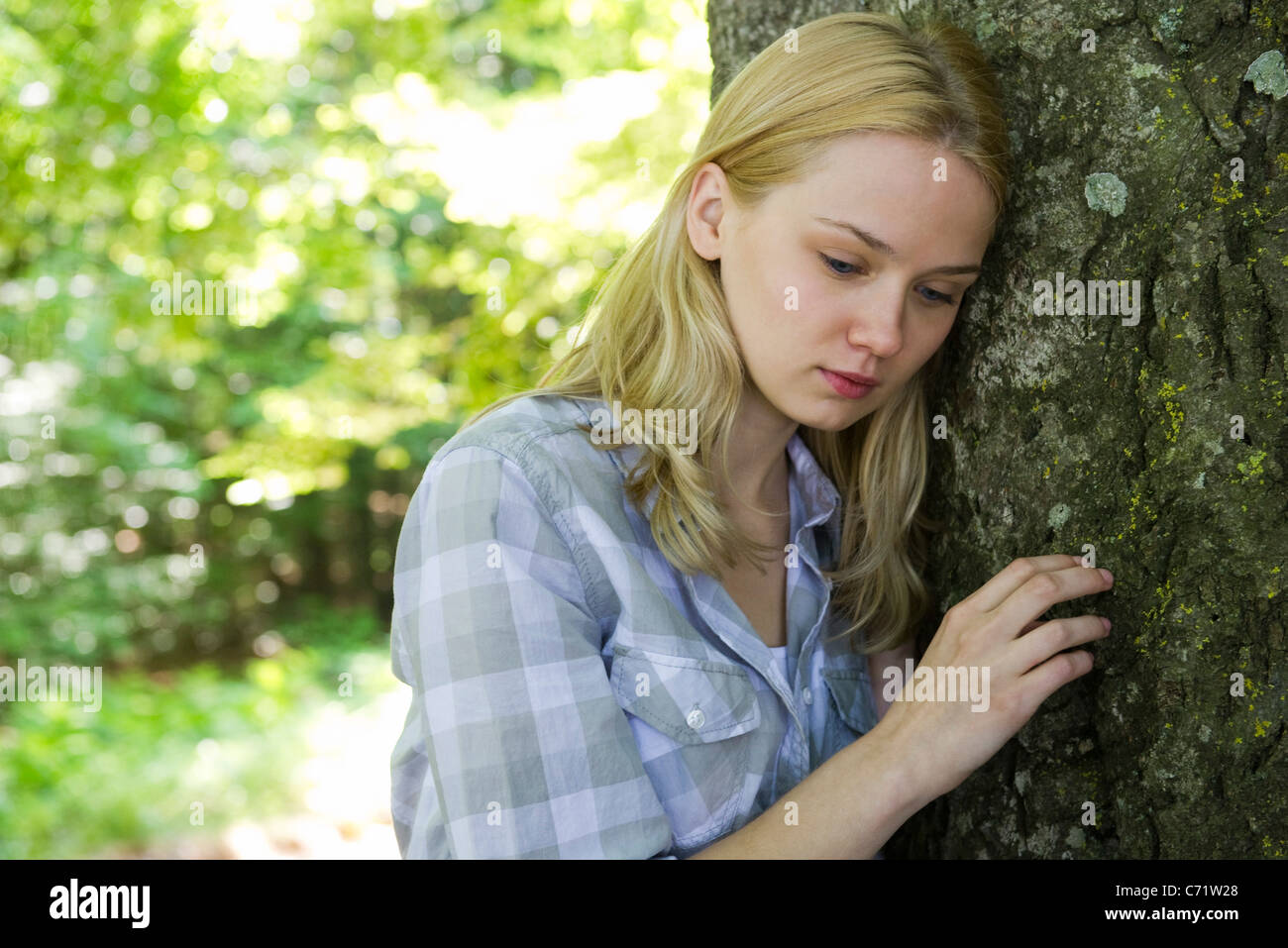 Young woman leaning against tree, looking sad Stock Photo - Alamy
