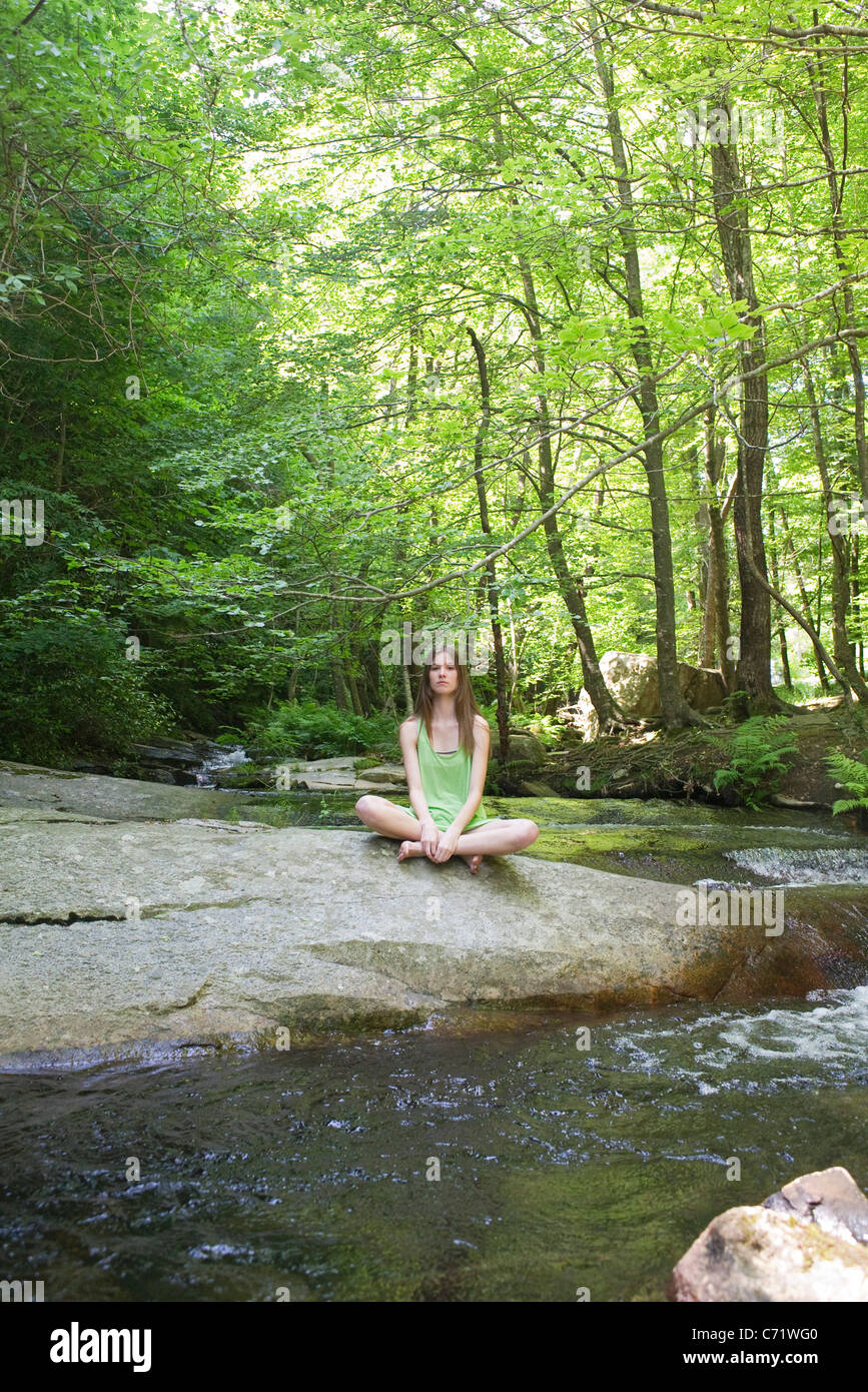 Young woman sitting on rock beside stream Stock Photo - Alamy
