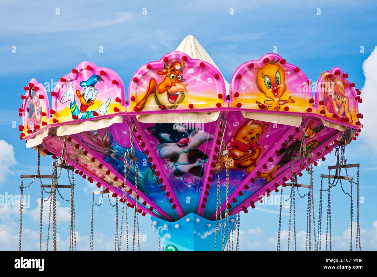 Brightly coloured pink top of a fairground ride or carousel against a ...