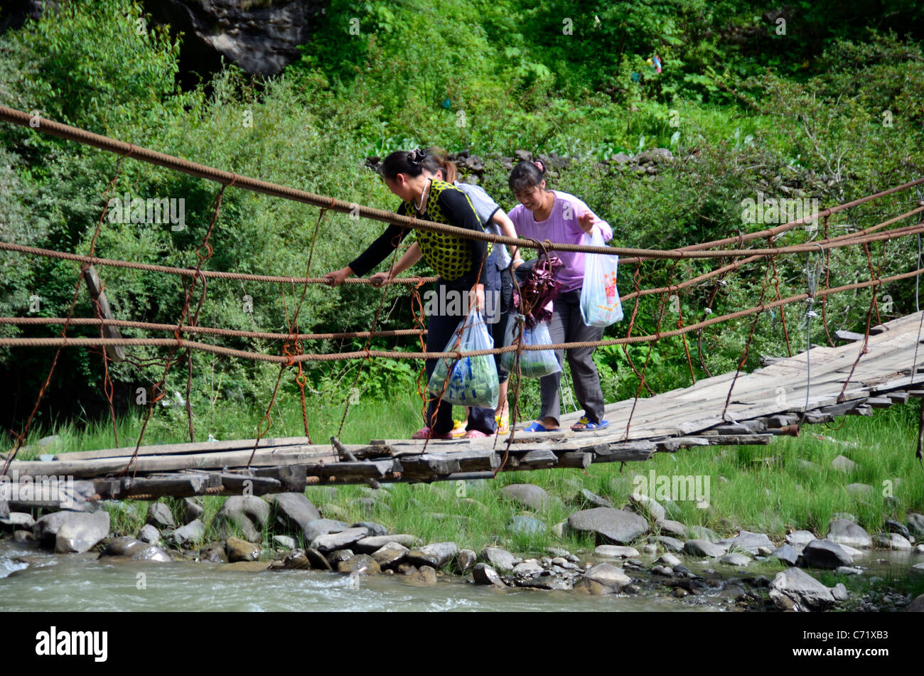 Three young women are nervous of crossing a primitive hanging bridge ...