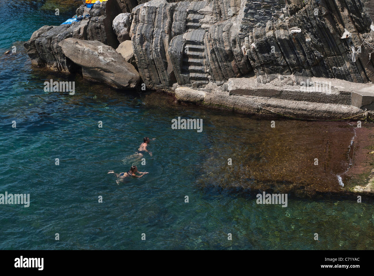 Young Italian adults sunbath and swim in the harbor of Riomaggiore ...