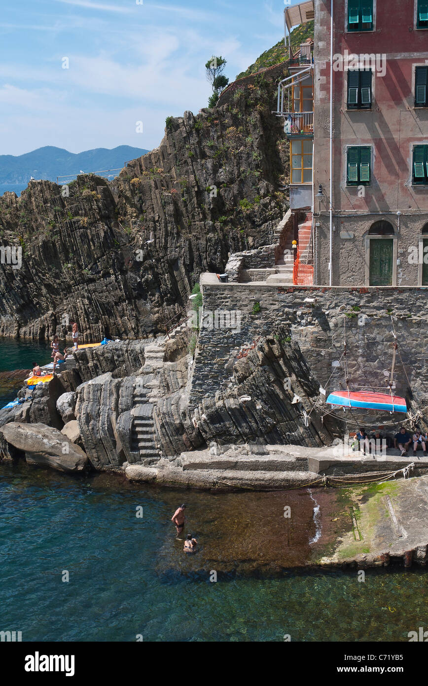 Young Italian adults sunbath and swim in the harbor of Riomaggiore ...