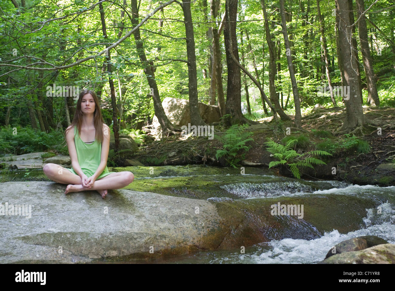 Young woman sitting on rock beside stream Stock Photo - Alamy