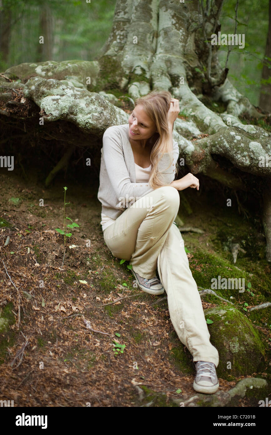 Woman sitting at base of tree in woods Stock Photo - Alamy