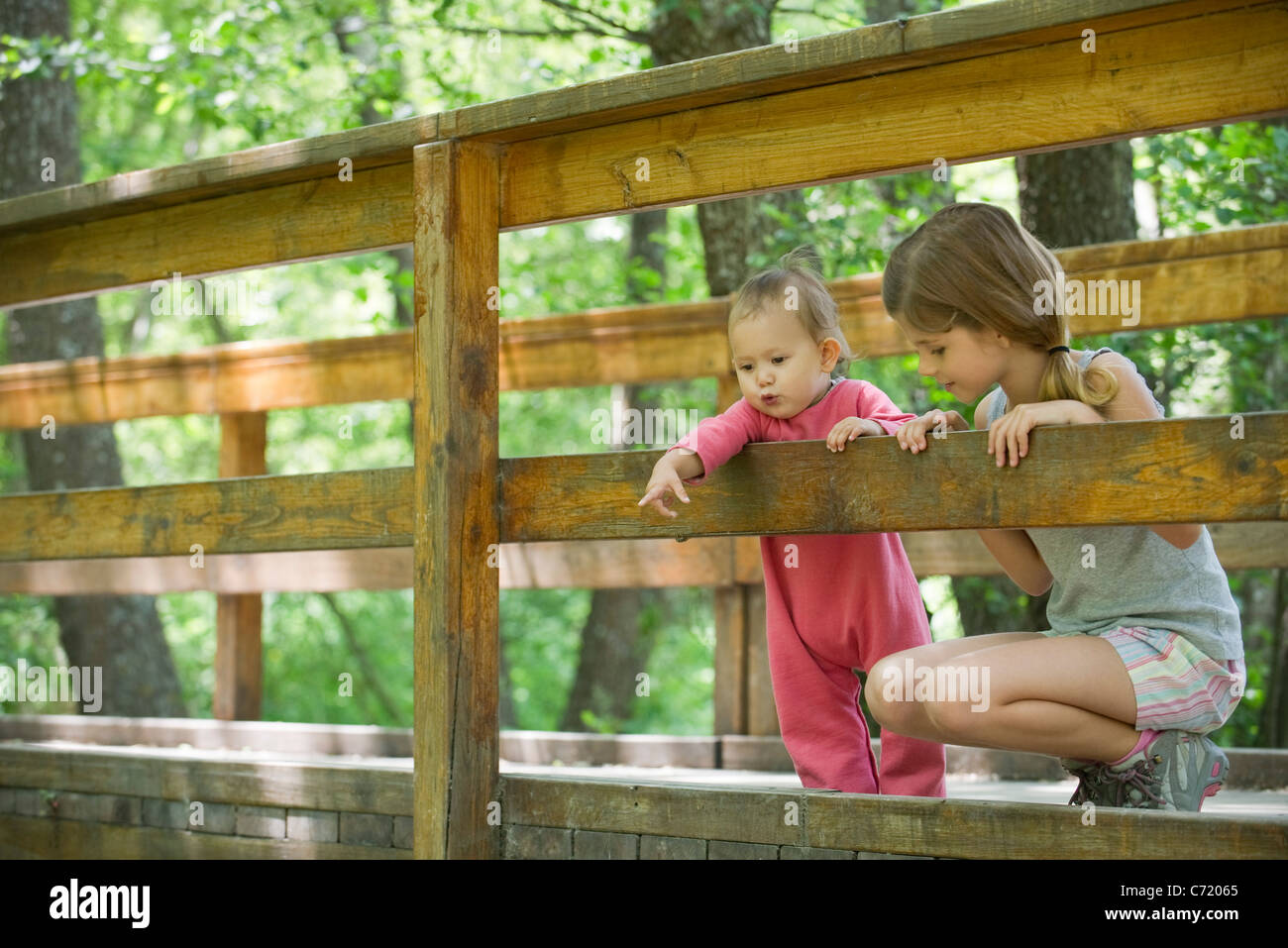 Baby girl and older sister looking over railing of bridge Stock Photo ...