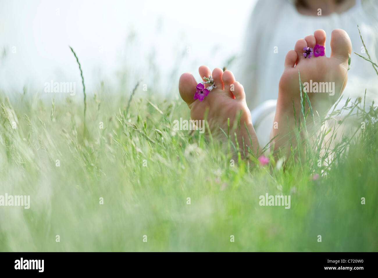 Barefoot young woman sitting in grass with wildflowers between toes ...