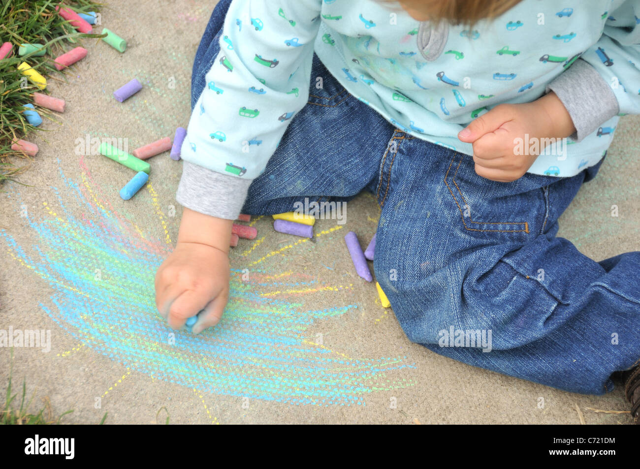 A child holding a chalk crayon drawing outdoor surrounded by colourful ...