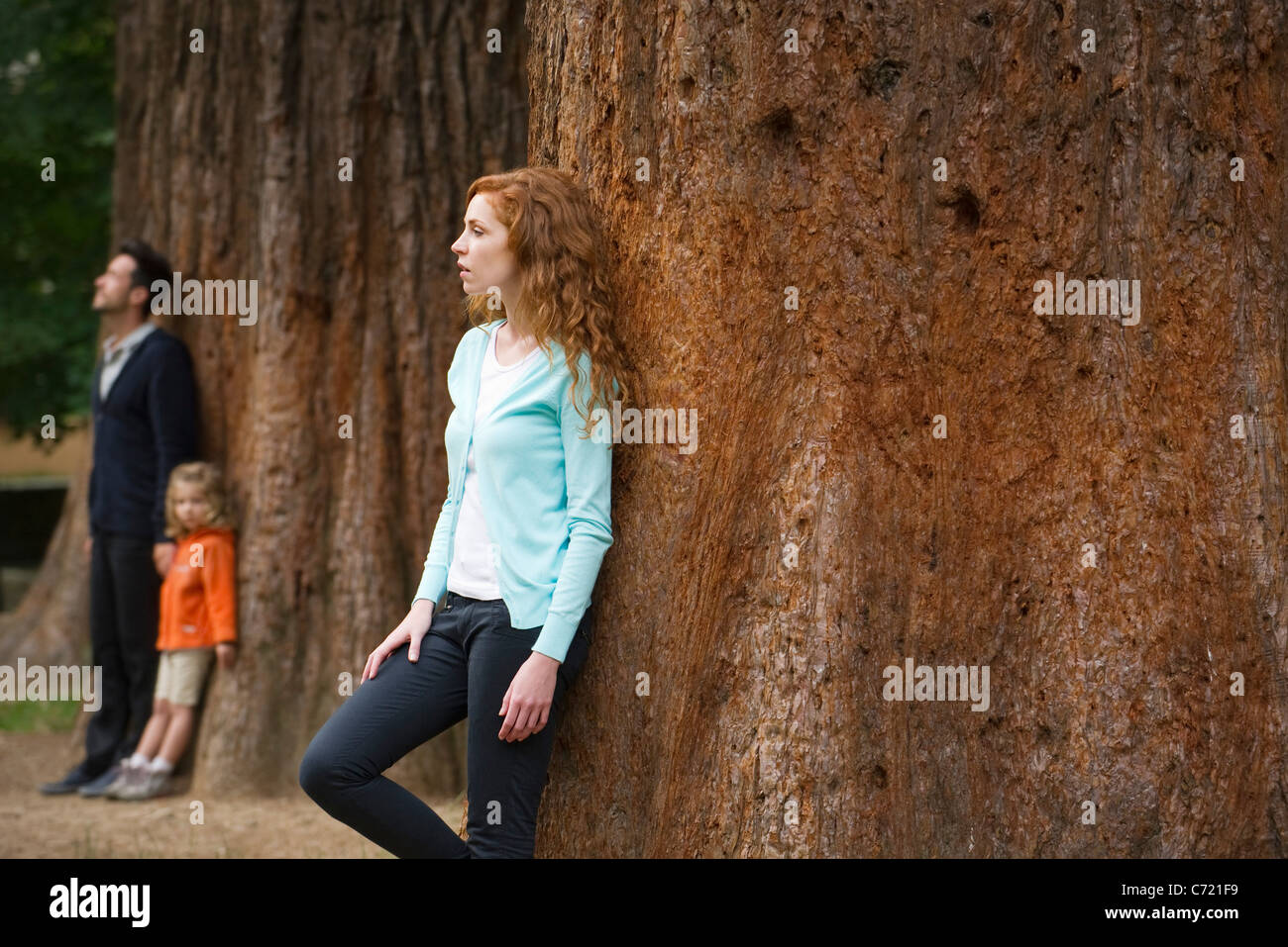 Mother leaning against tree trunk, husband and daughter separate in ...