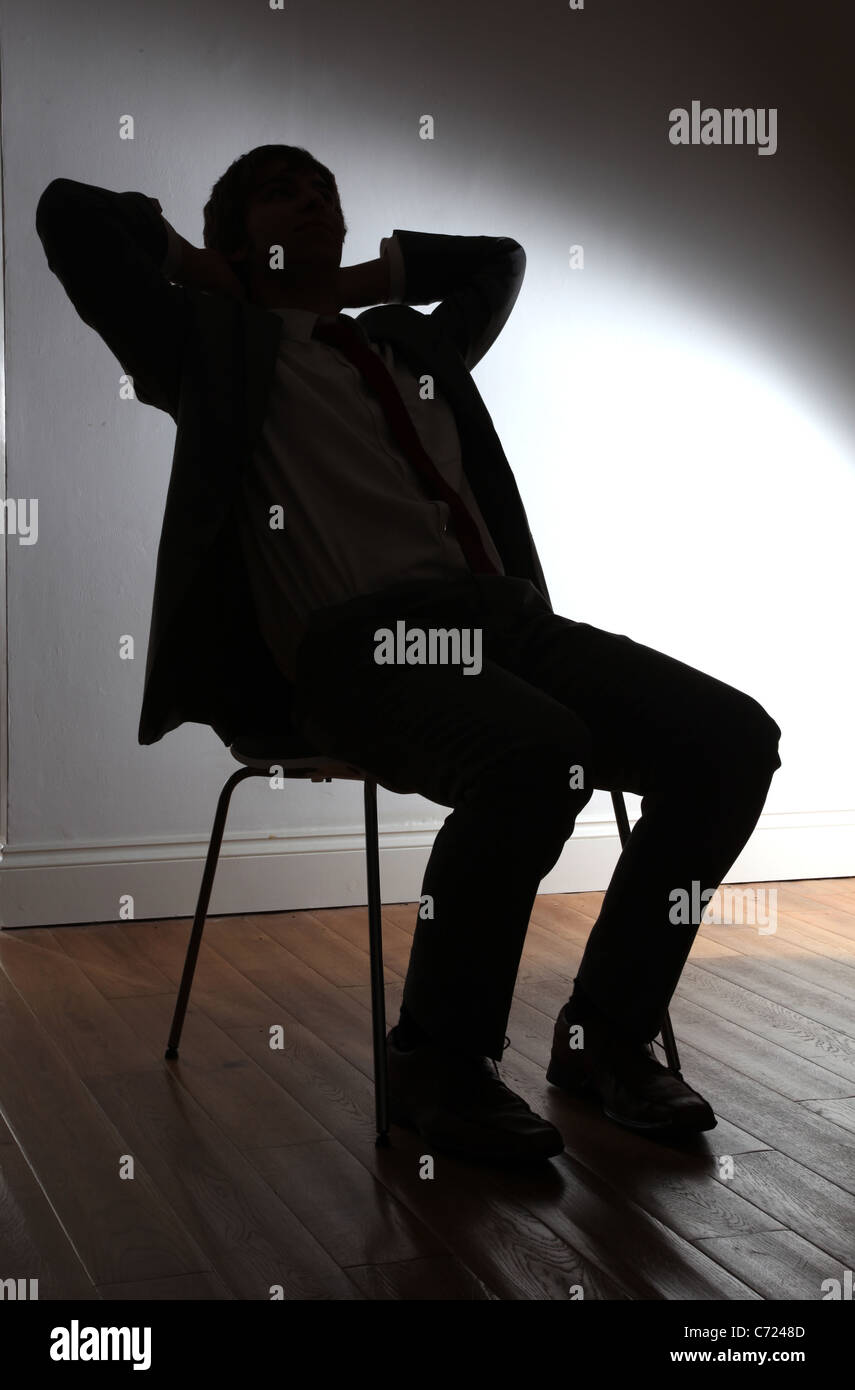 Silhouette of a young male sitting in a chair with his hands behind his ...
