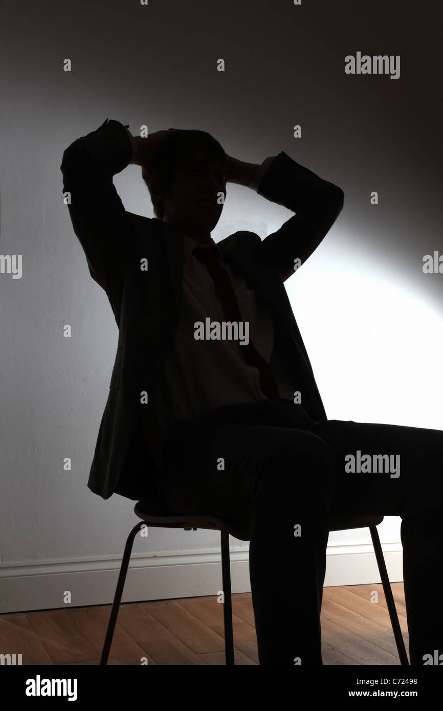 Silhouette of a young male sitting in a chair with his hands behind his ...