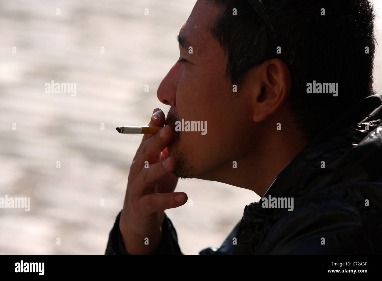 A man (sitting on the ground) puffing on a lighted cigarette Stock ...