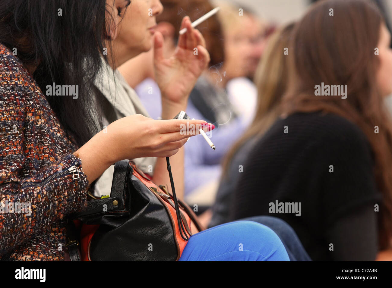 Two ladies sitting in a crowd, each holding a cigarette Stock Photo - Alamy
