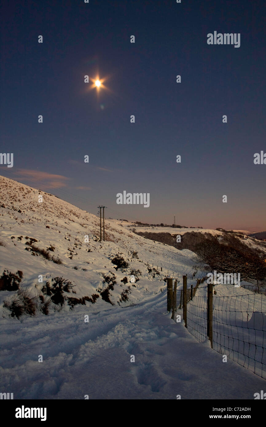 a snow covered farm road lit by moonlight. with mountains in the ...