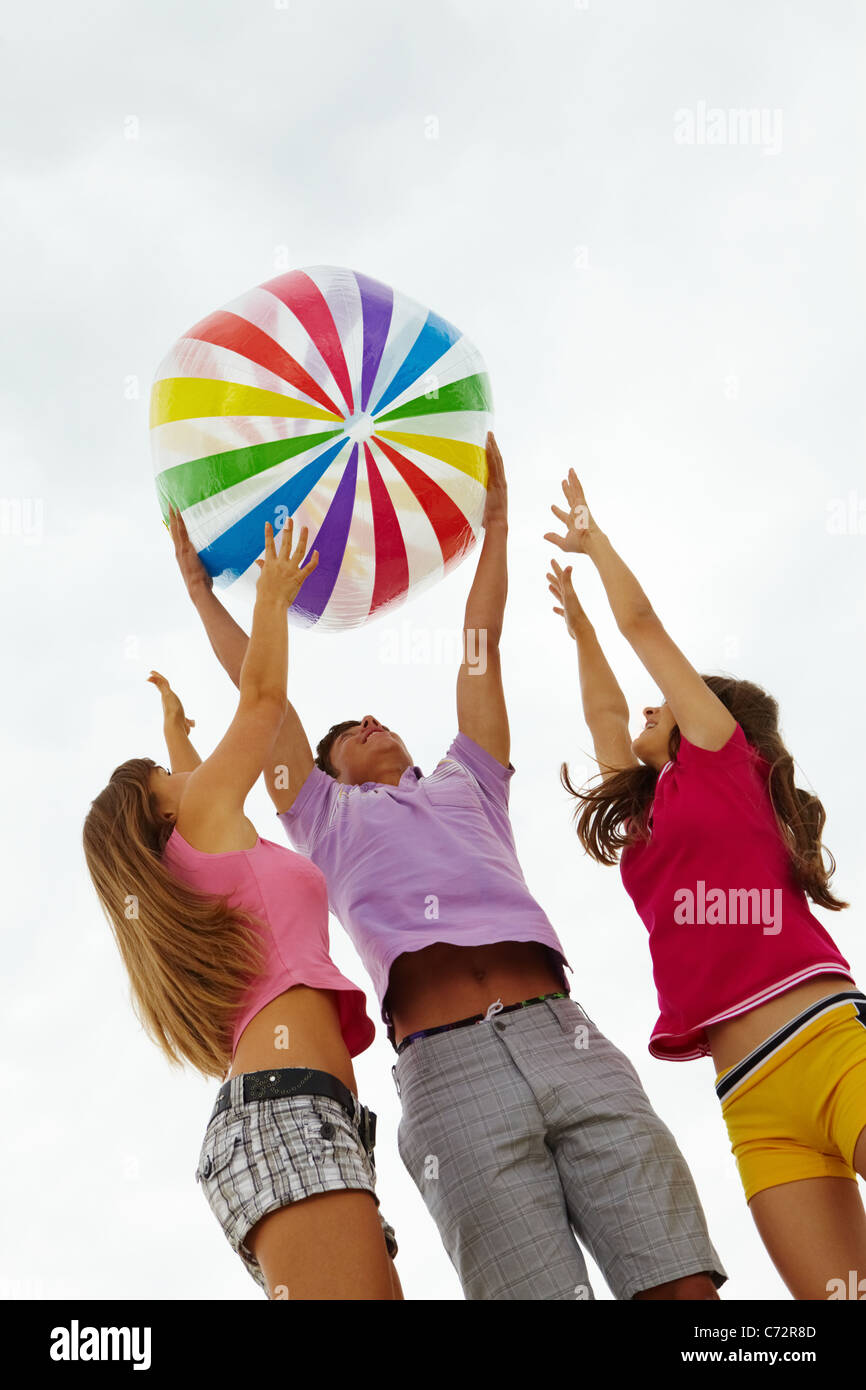 Photo of teenage friends playing with ball on background of cloudy sky ...