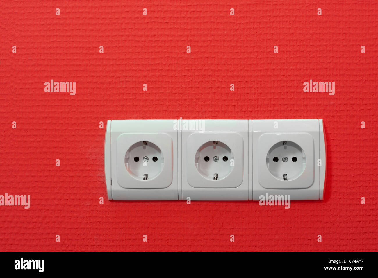 Three empty electric sockets on red wall Stock Photo - Alamy