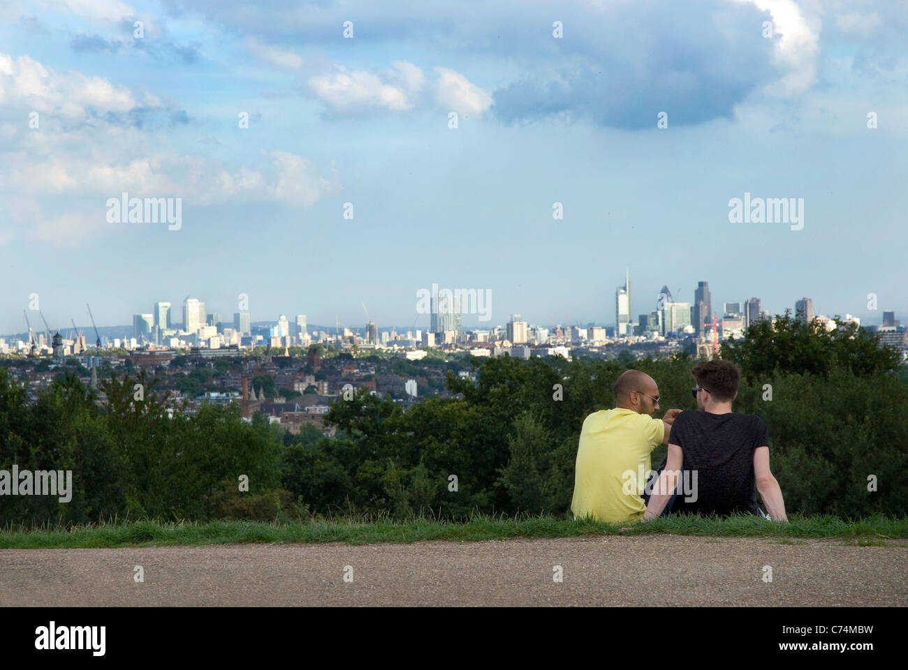 Two men sit talking together on Parliament Hill overlooking London with ...