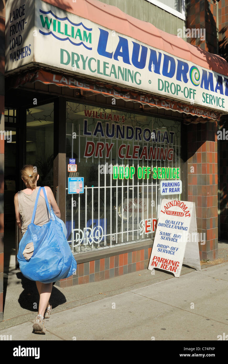 Female customer carrying her laundry entering a public laundromat ...
