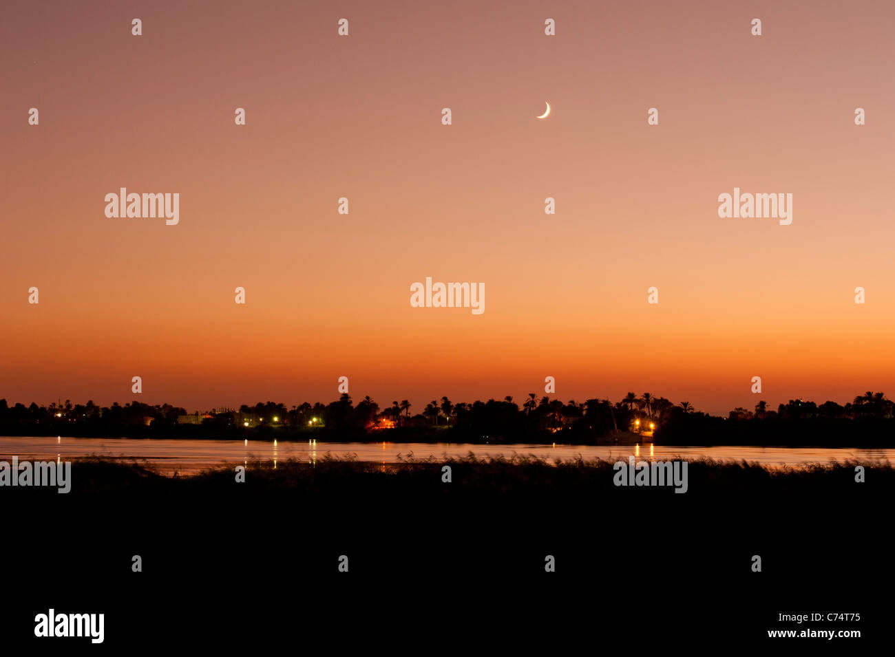 Orange sunset sky with the moon over a large river Stock Photo - Alamy