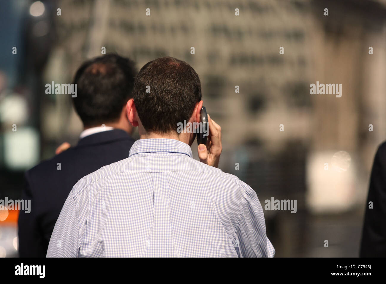 the rear view of a man using a mobile phone while walking in a street ...