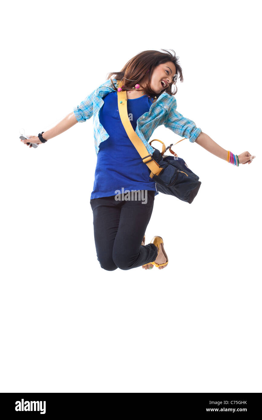 Beautiful college woman jumping while listening music over white ...