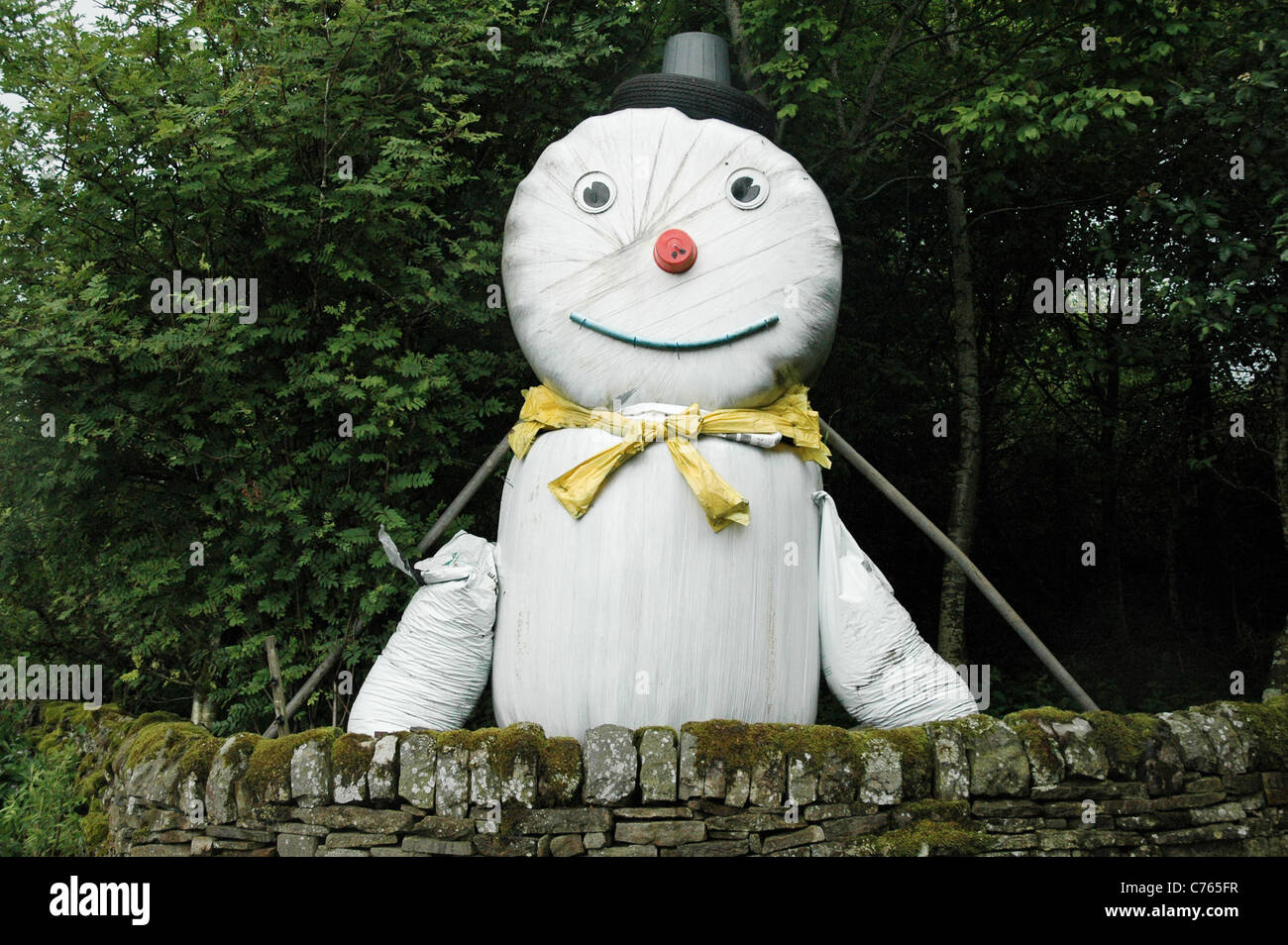 A large smiling scarecrow made of round hay bales stands guard on a ...