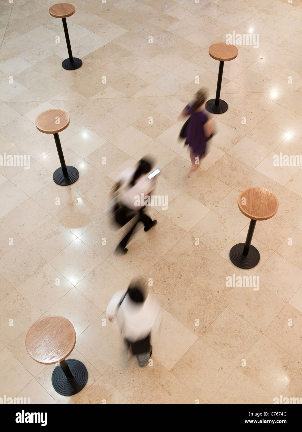 A view from above of three blurred people walking amongst five tables ...