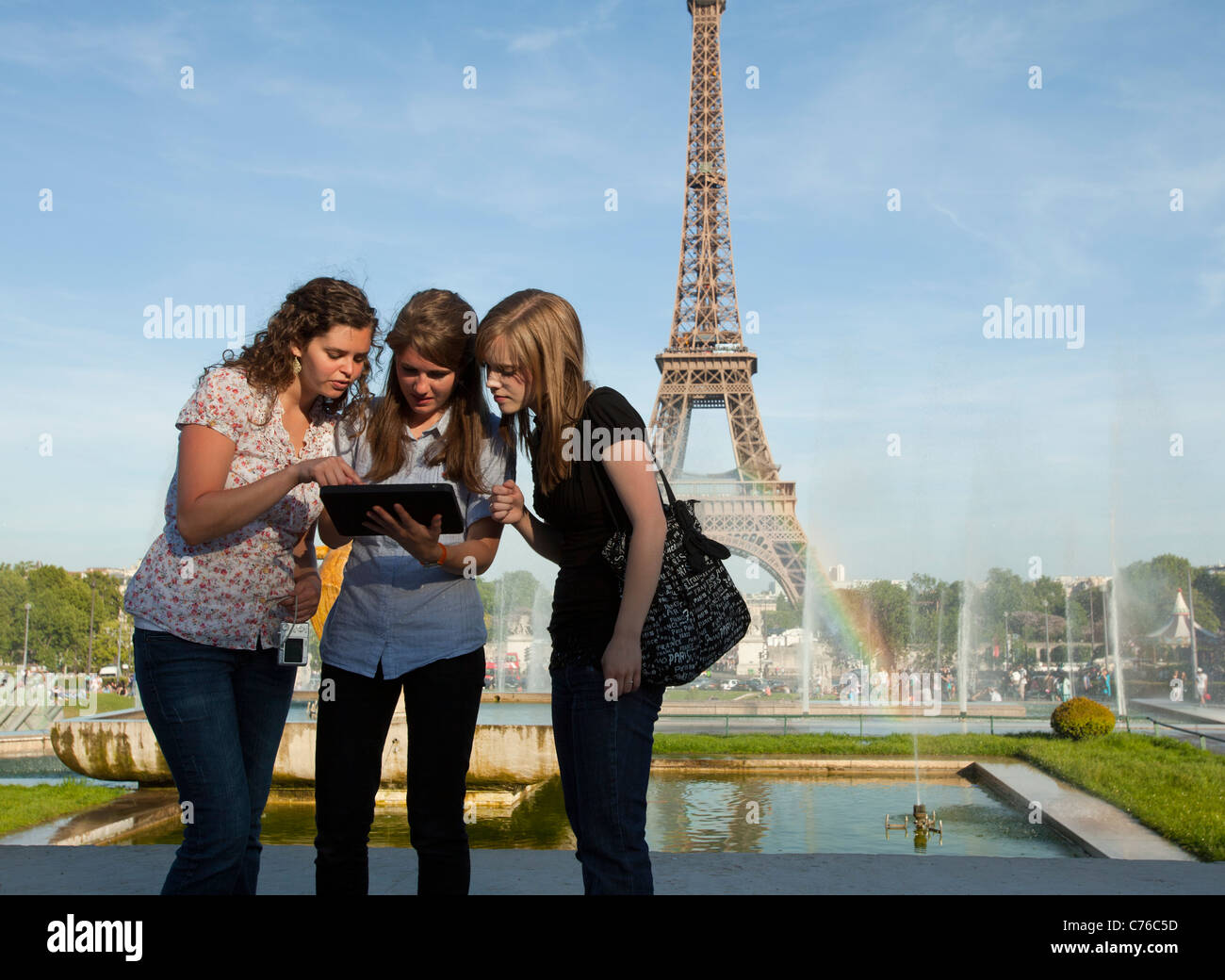 France, Paris, Three young women using tablet in front of Eiffel Tower ...