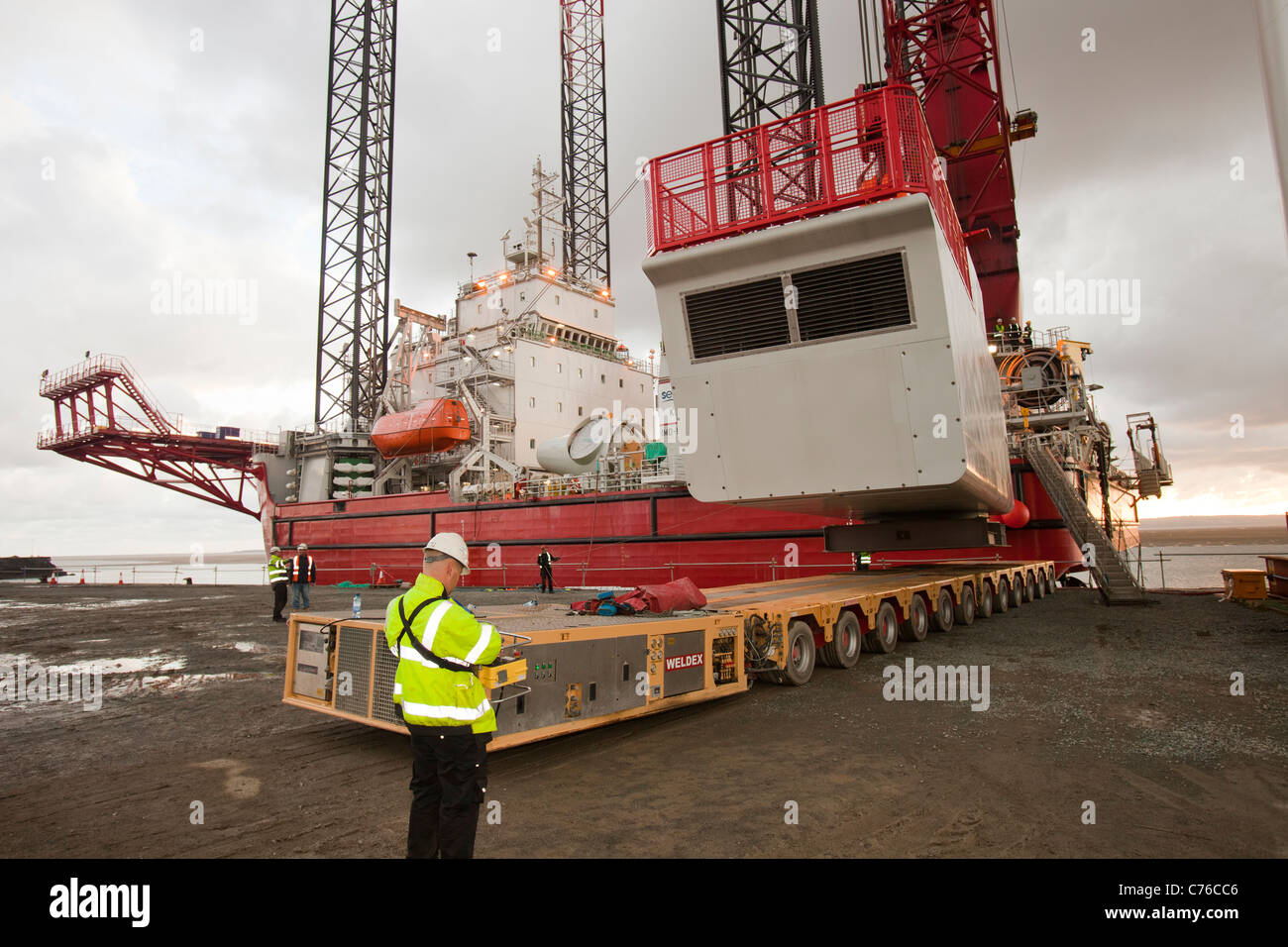 Workers lift a nacelle for a wind turbine onto a jack up barge, for the ...