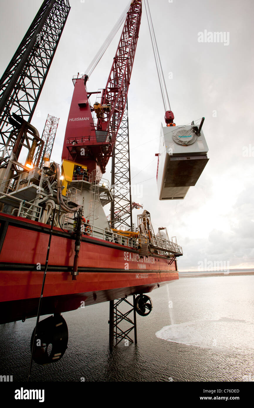 Workers lift a nacelle for a wind turbine onto a jack up barge, for the ...