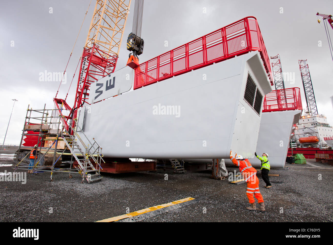 Workers lift a nacelle for a wind turbine onto a jack up barge, for the ...