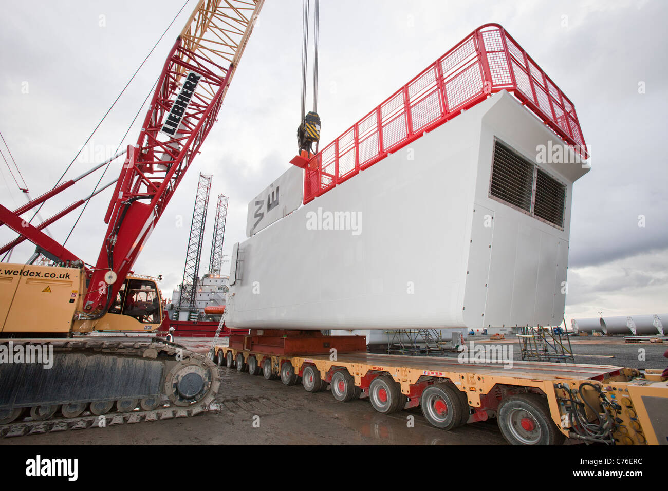 workers prepare to lift a nacelle of a wind turbine onto a jack up ...
